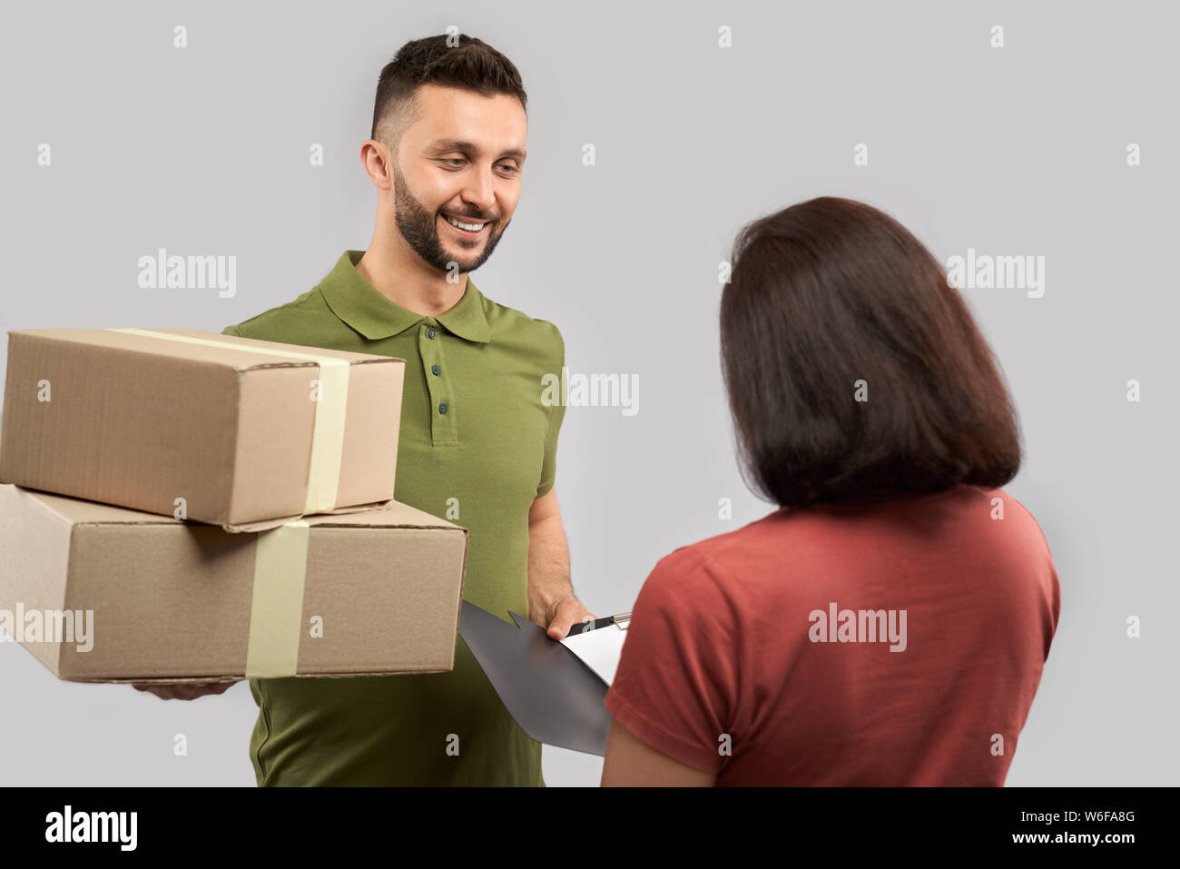Young, handsome, smiling delivery man standing and holding two ...