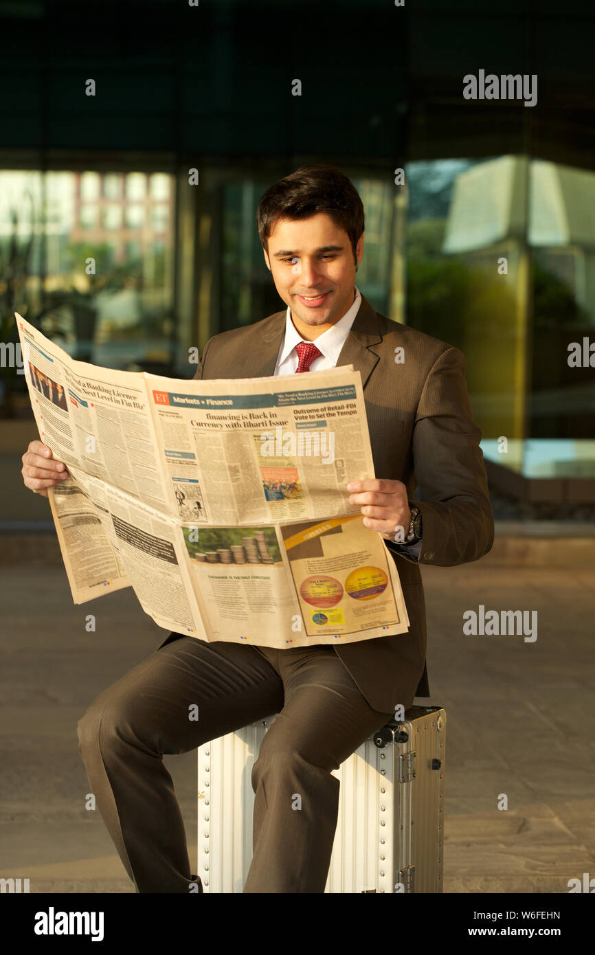 Businessman reading a newspaper at an airport Stock Photo - Alamy