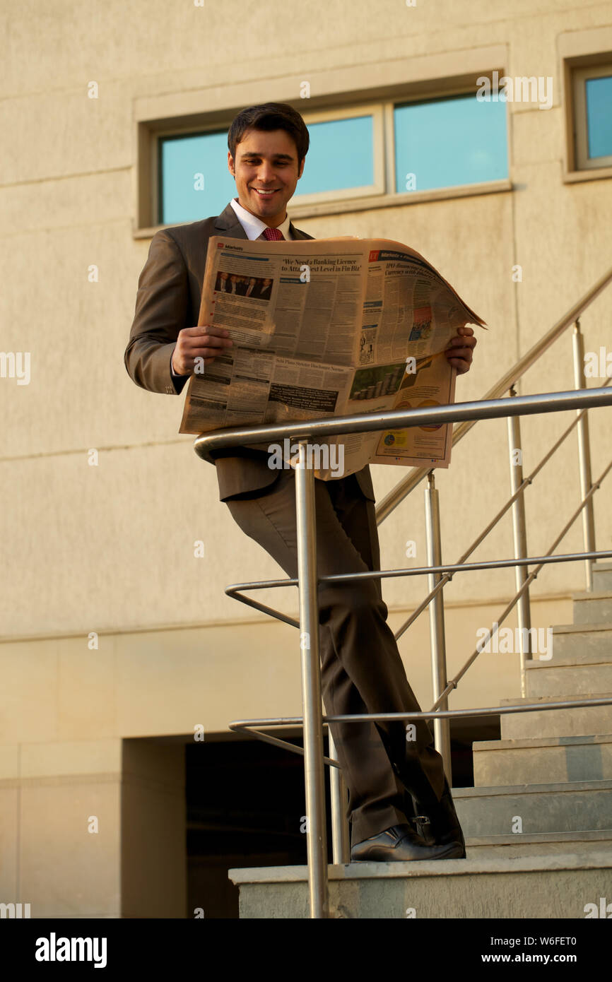 Businessman leaning against railing and reading newspaper Stock Photo ...