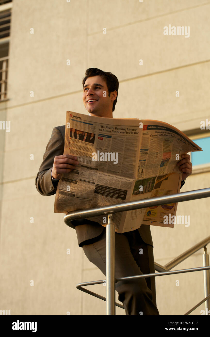 Businessman leaning against railing and reading newspaper Stock Photo ...
