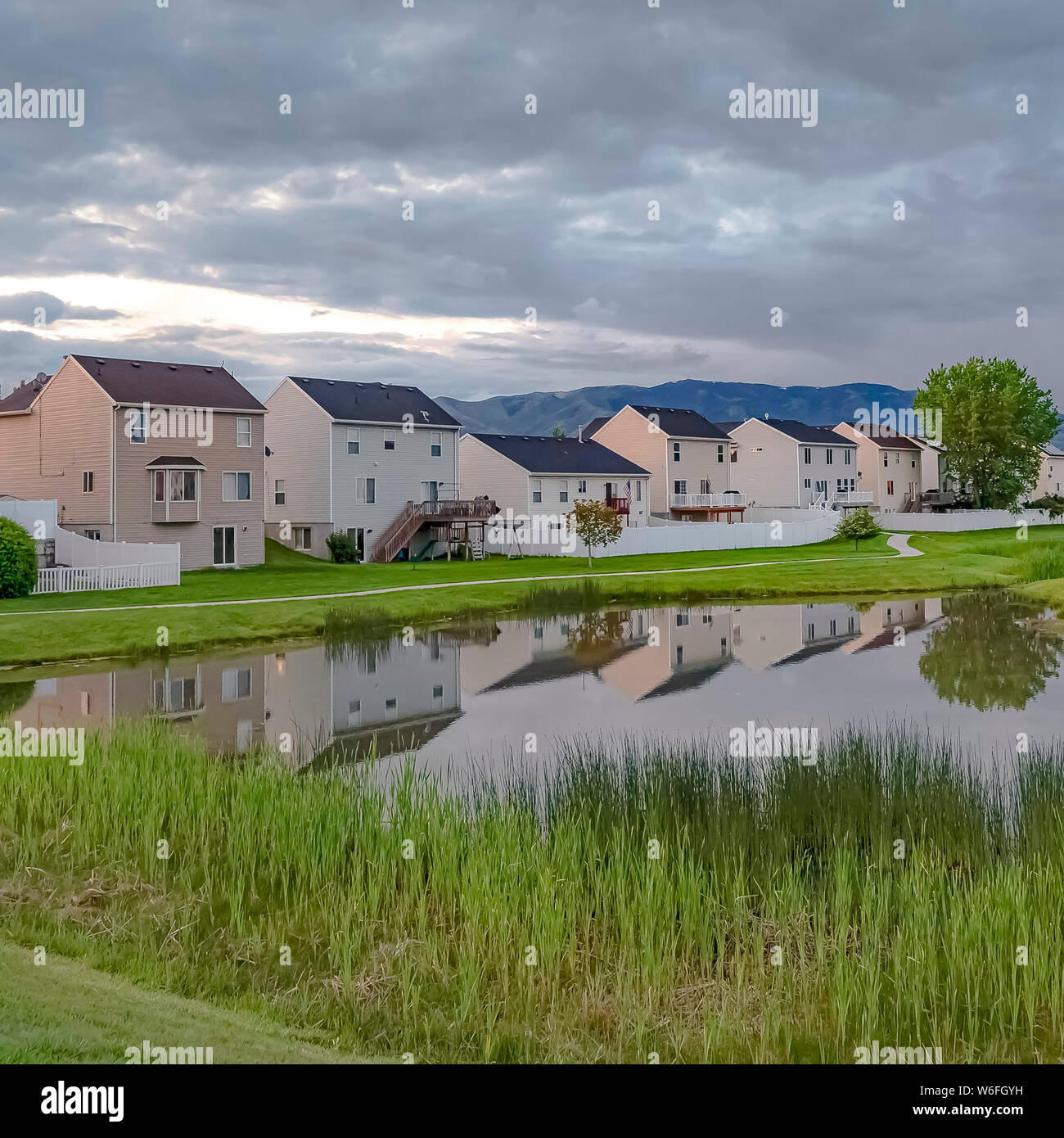 Square Shiny pond with bridge on a grassy park in front of lovely homes ...