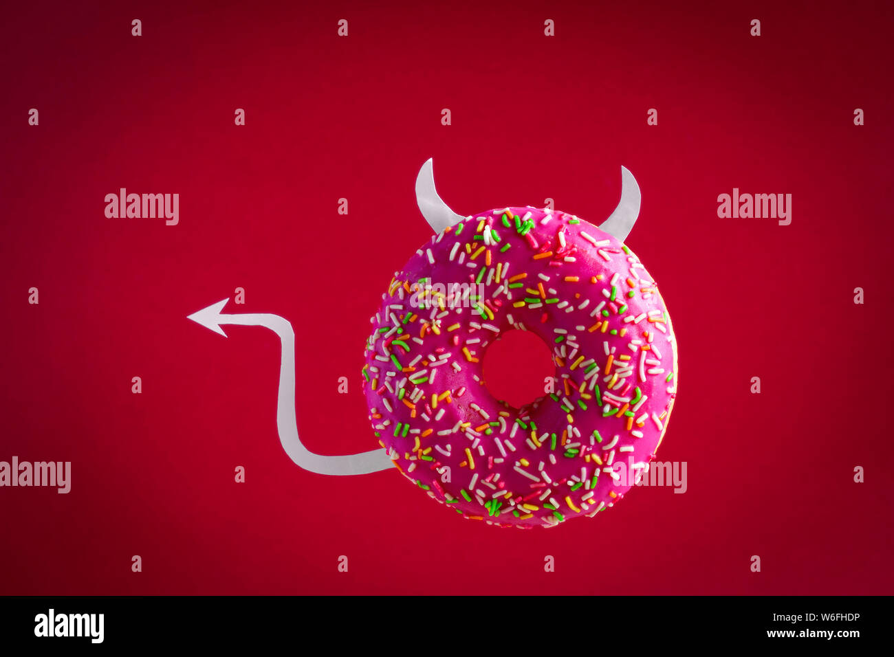 devil donut with paper horns and tail flying on red background Stock ...