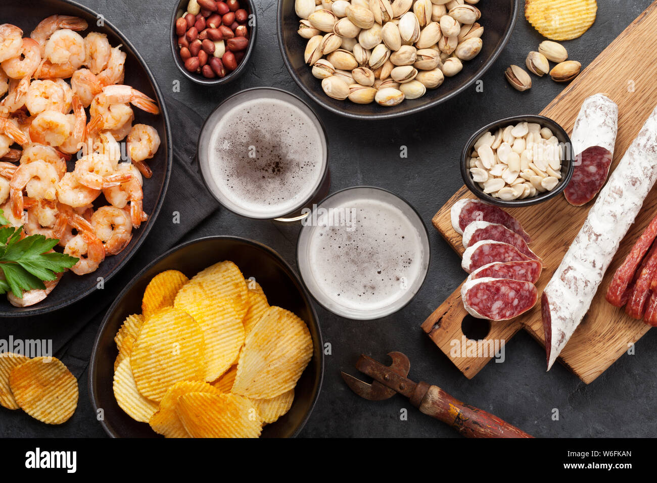 Draft beer and snacks on stone background. Nuts, chips, sausages and ...