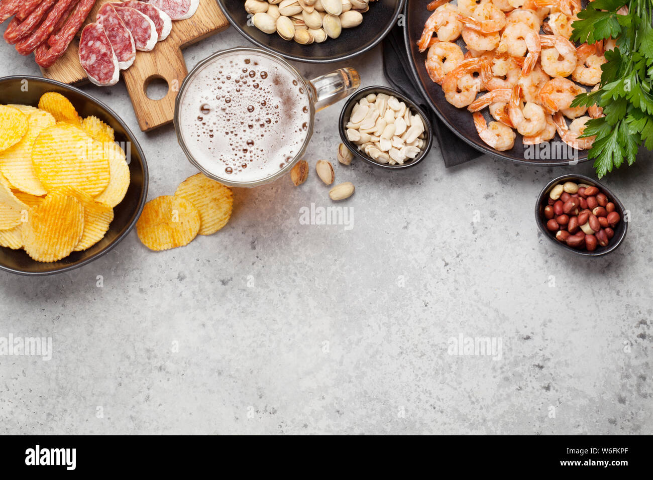 Draft beer and snacks on stone background. Nuts, chips, sausages and ...