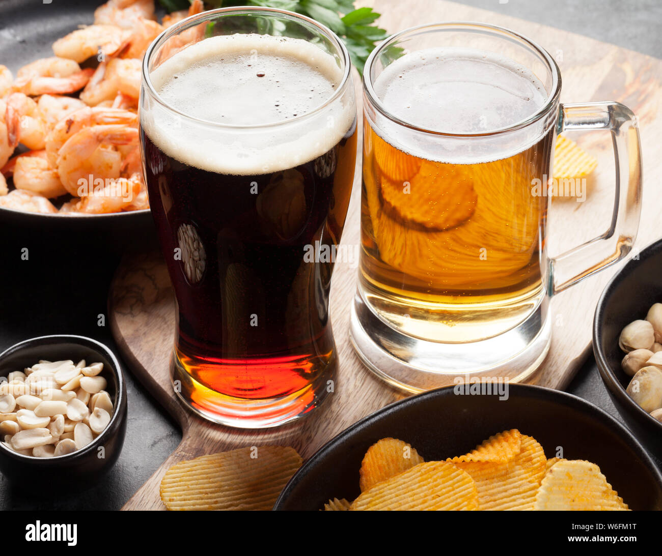 Draft beer and snacks on stone background. Nuts, chips, sausages and ...