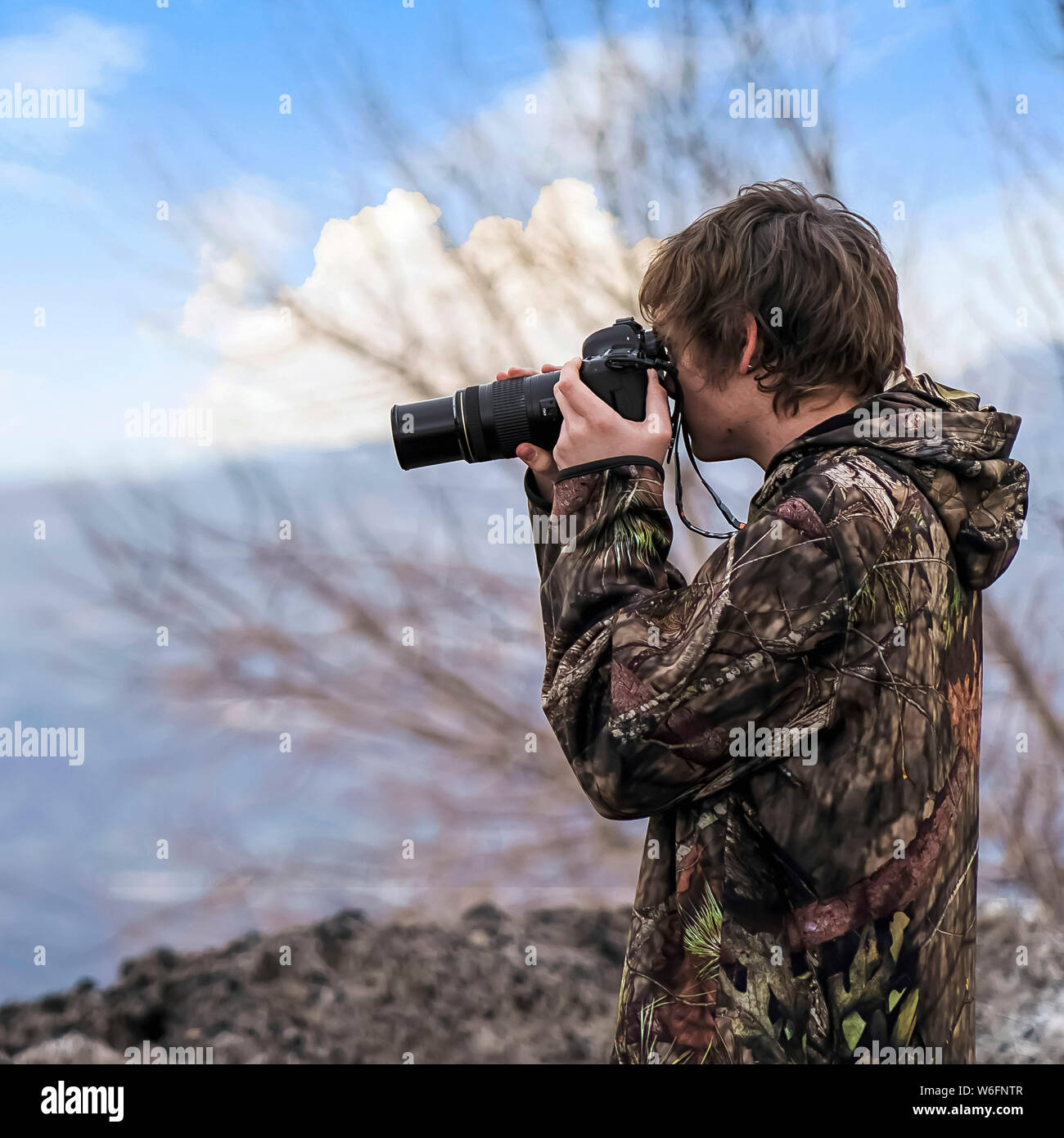 Side view of a man holding a camera with tree and cloudy blue sky ...