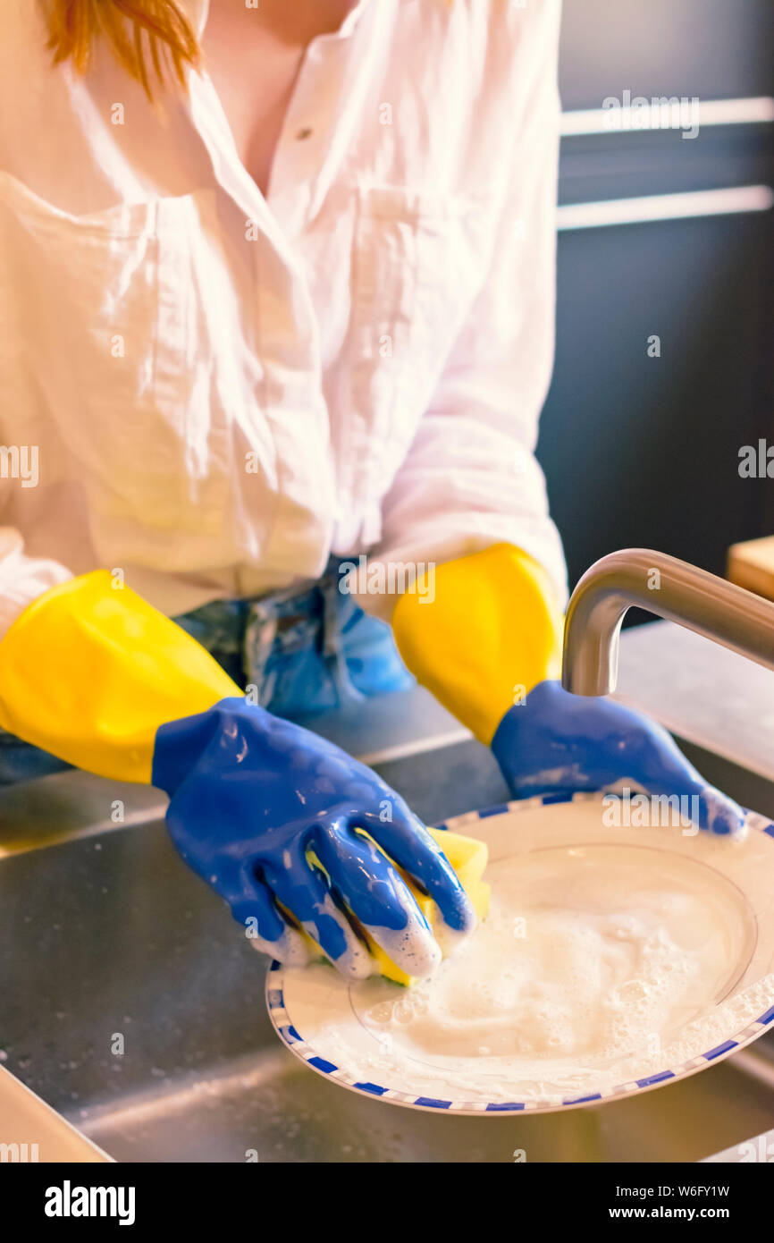 Young woman scrubbing a plate in a stainless steel sink, with yellow ...