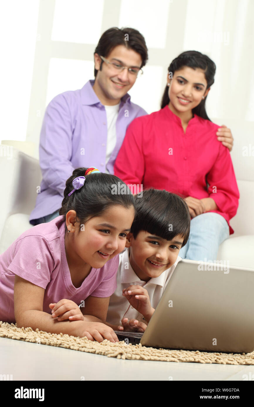 Children using laptop with their parents sitting on couch Stock Photo ...