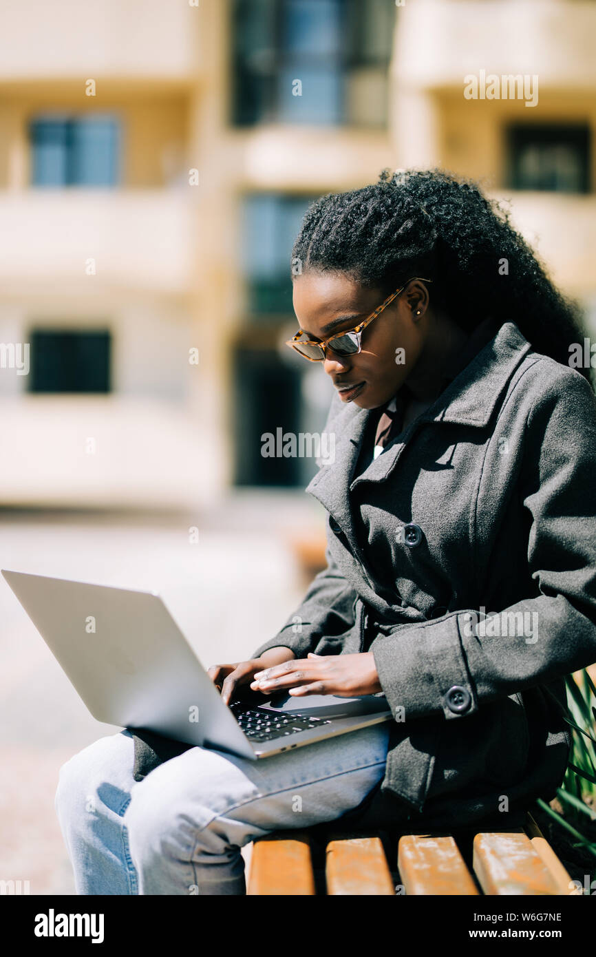 Smiling young African female university student sitting on a campus ...