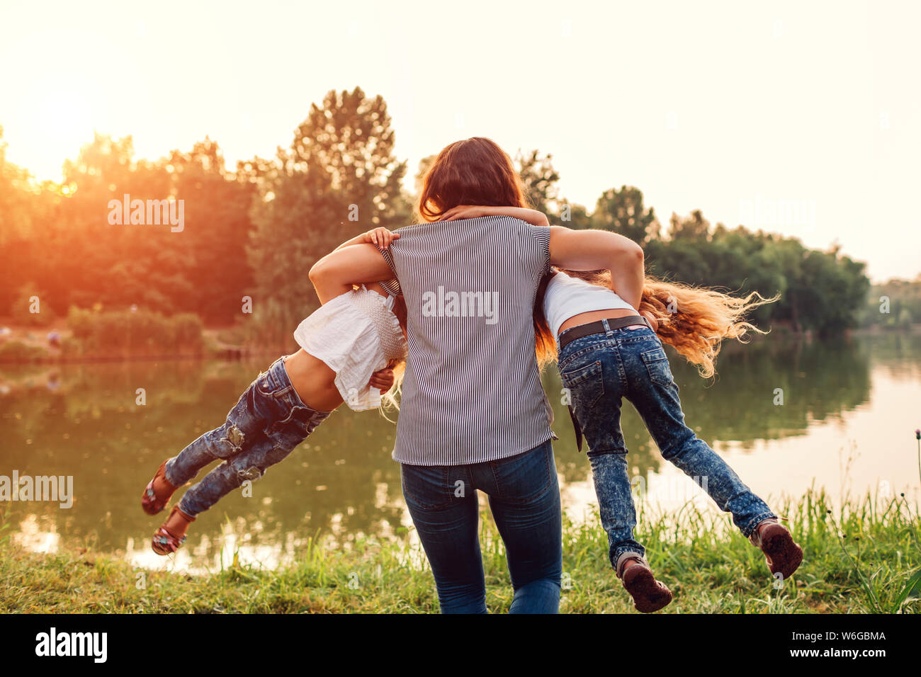 Family playing and having fun by summer river at sunset. Mother holding ...