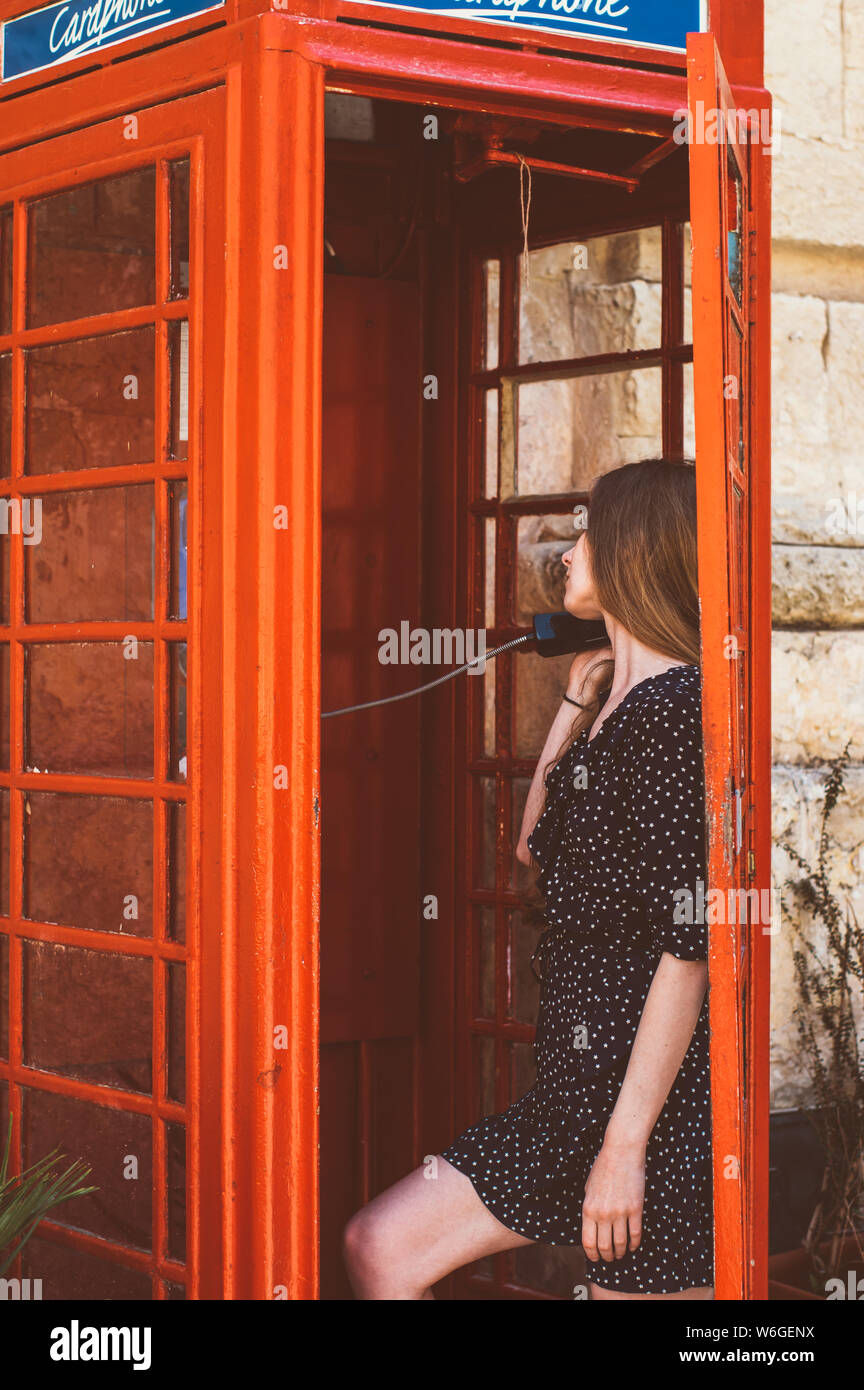 Young woman in red telephone cabin talking on the phone Stock Photo - Alamy