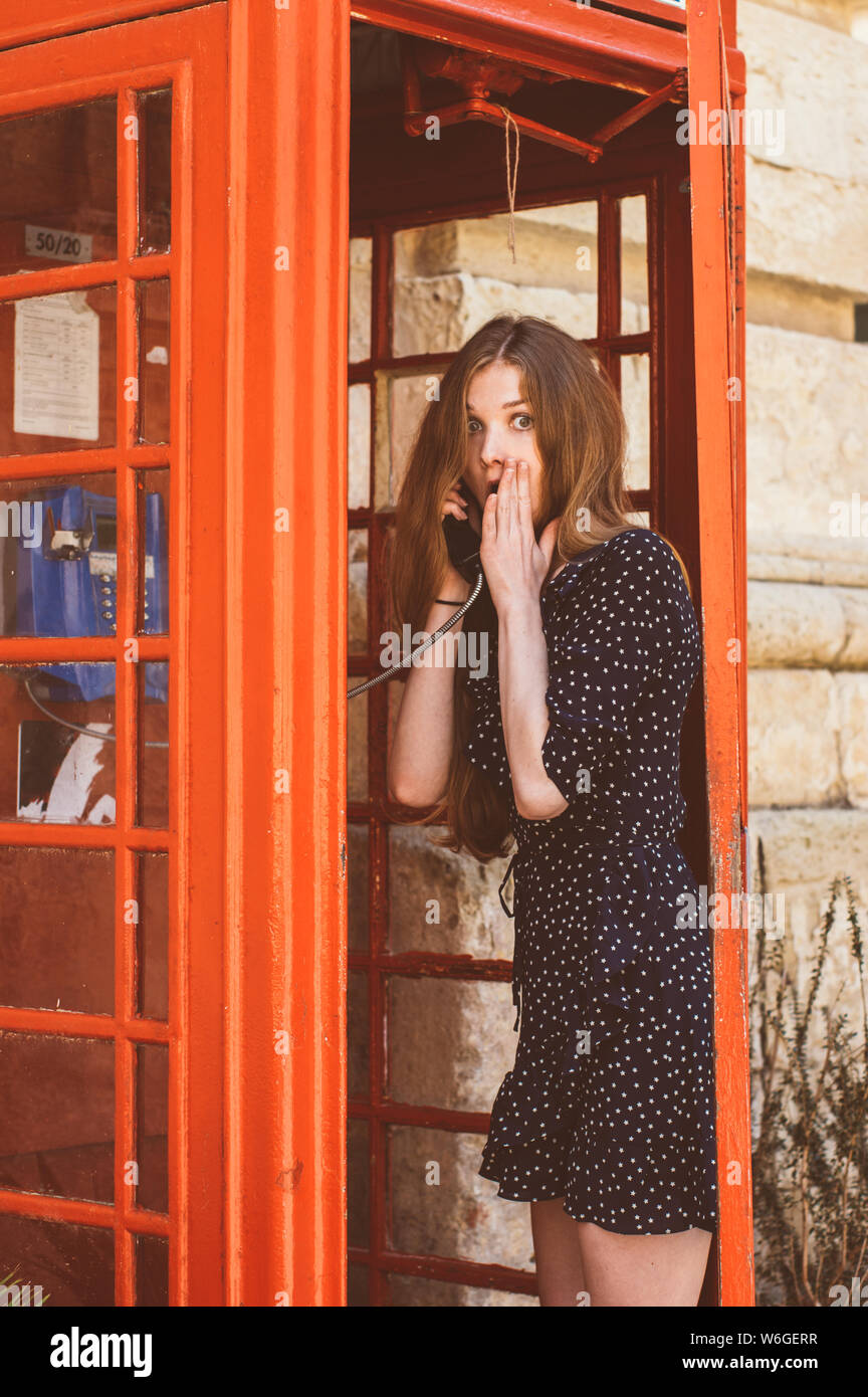 Young woman in red telephone cabin talking on the phone and surprising ...