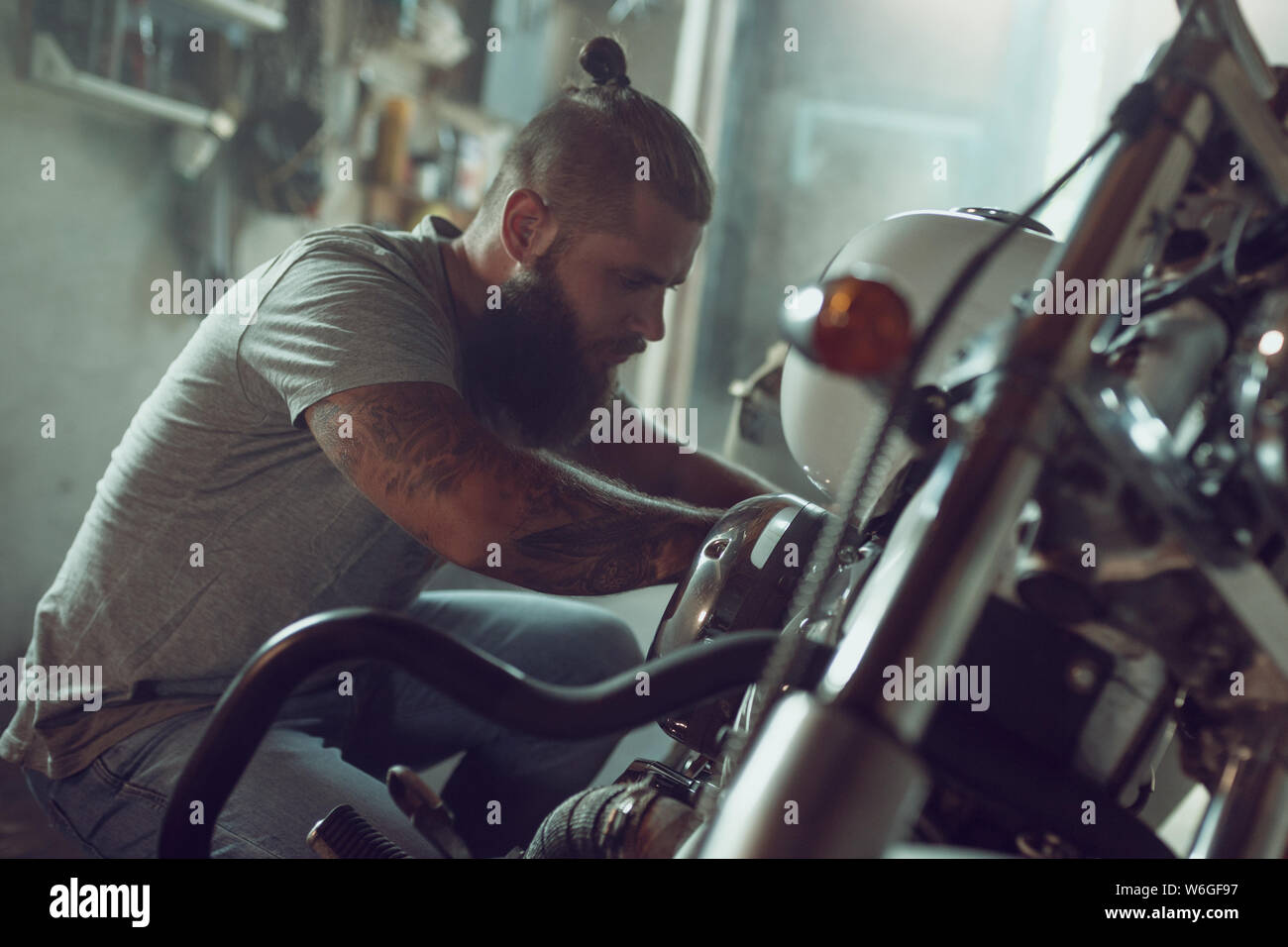 Handsome bearded man repairing his motorcycle in the garage. A man ...