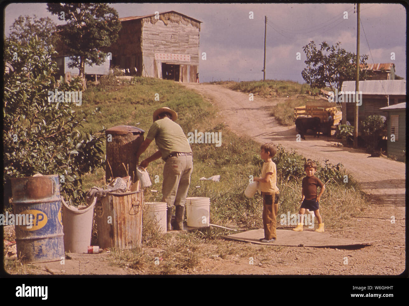 FATHER AND SONS FILL THEIR CONTAINERS AT THE COMMUNITY WATER PUMP. THIS ...