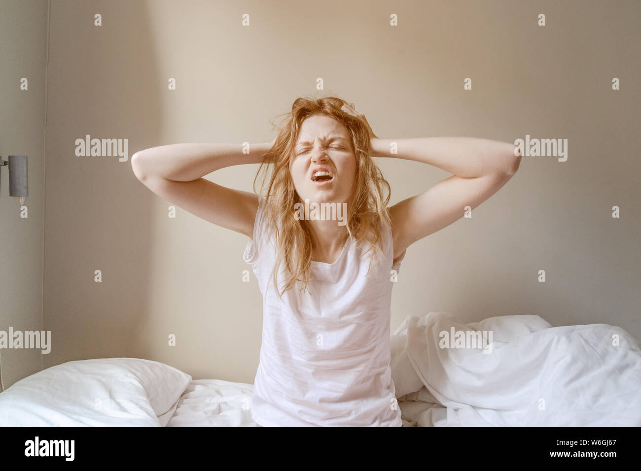Bad Morning. Frowning blonde in bed with hands on face. Young woman ...