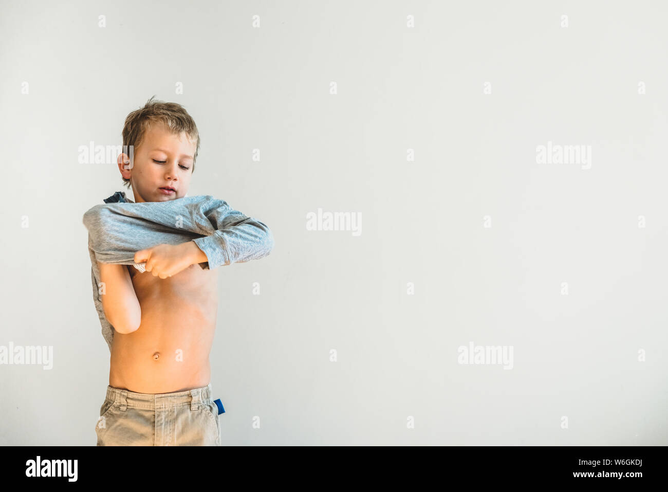 Child Trying To Take Off His Shirt And Undress On His Own Stock Photo child-trying-to-take-off-his-shirt-and-undress-on-his-own-stock-photo