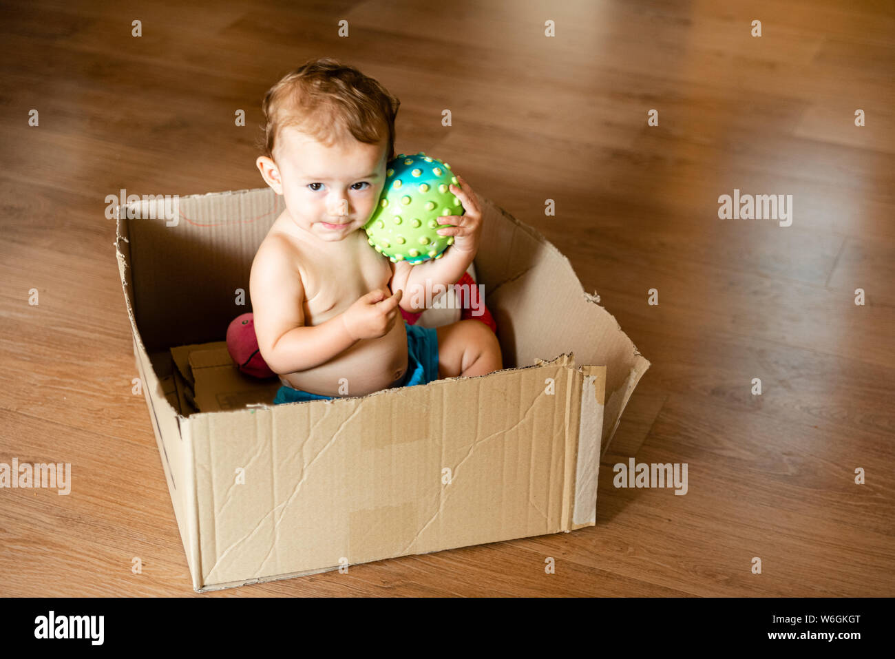 Baby girl playing with a ball inside a cardboard box and making an ...