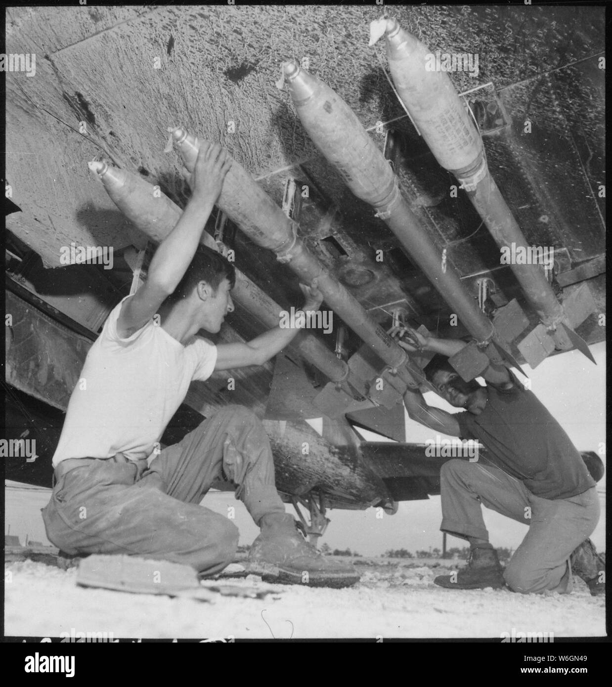 Five-inch rockets being loaded under the wing of an F4U of MAG-33. Just ...