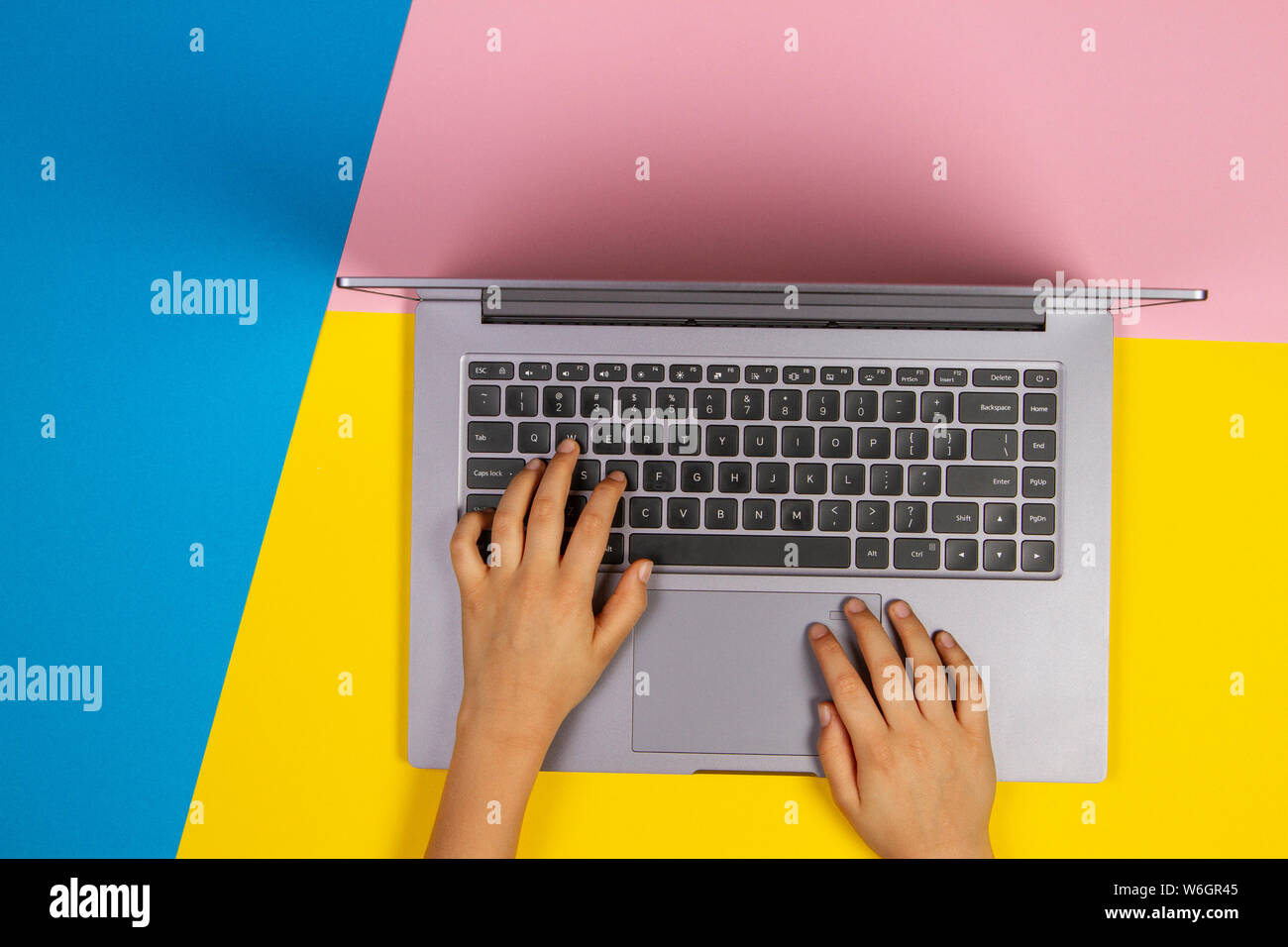 Kid hands typing on laptop computer keyboard on blue, yellow and pink ...
