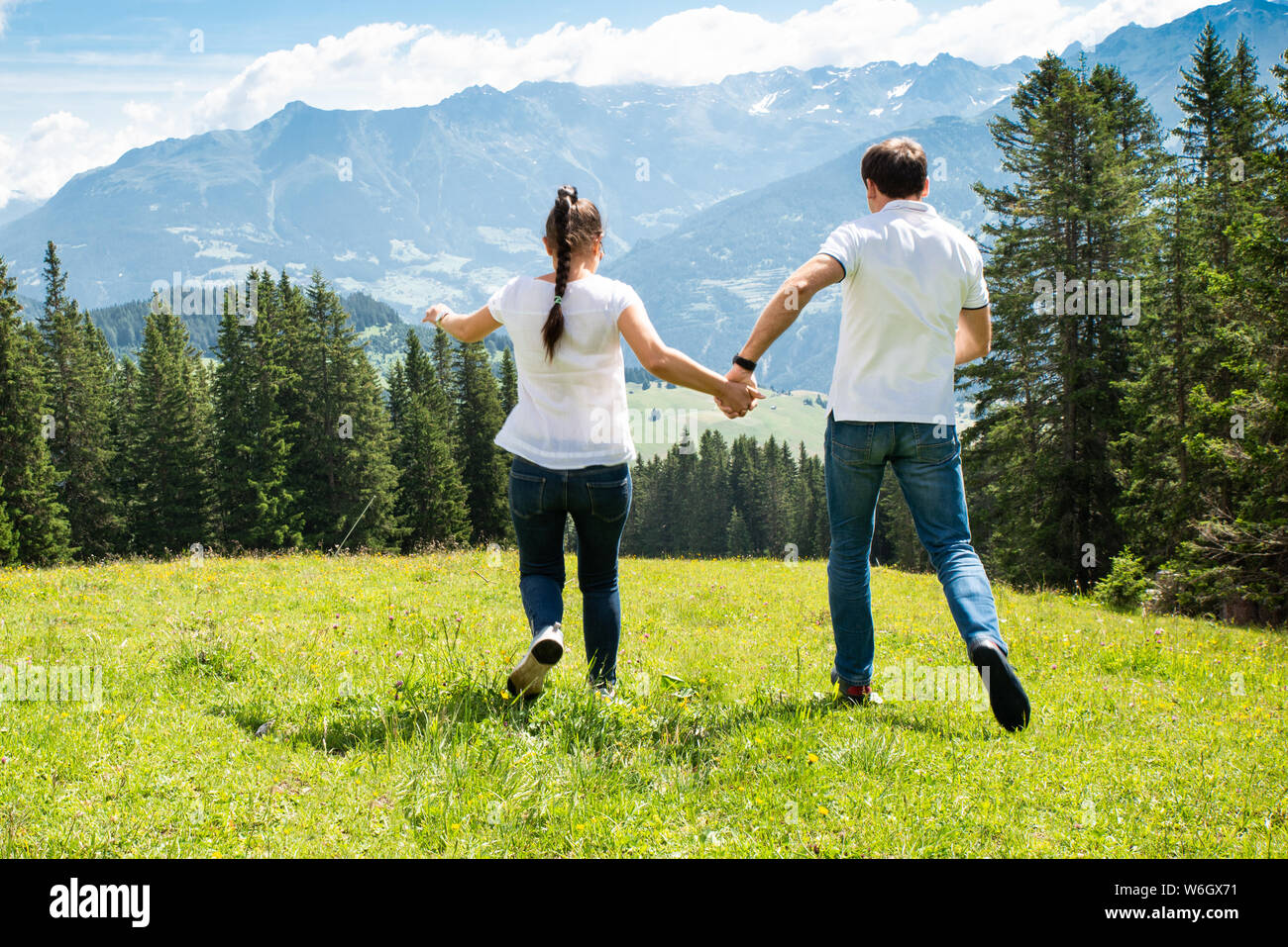 Couple Holding Hands Running On Field In Mountains Stock Photo - Alamy