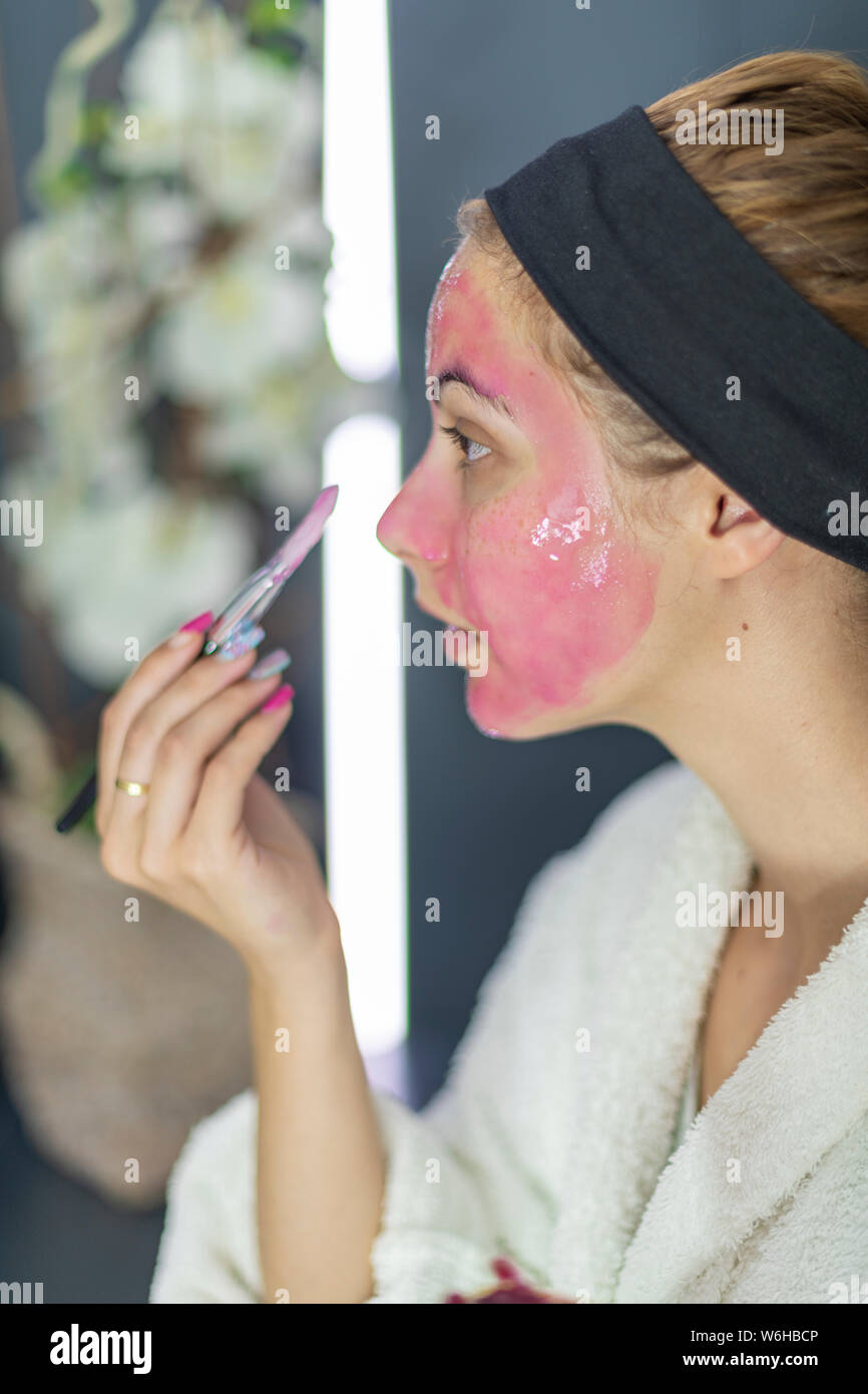 Side view of a white girl who applies a pink mask to her face - Organic ...
