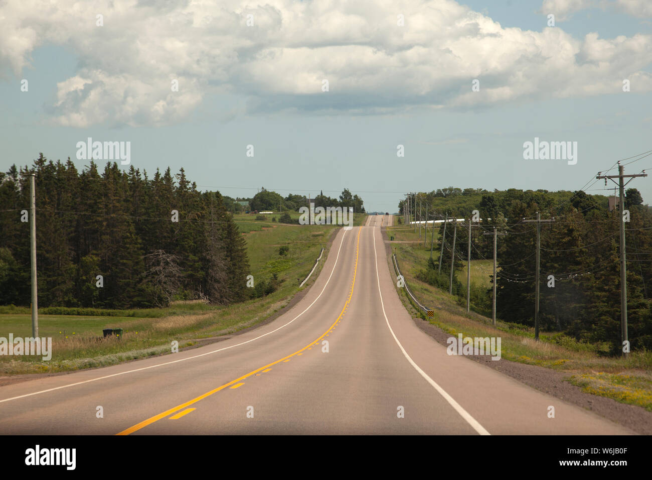 Long paved road in a rural area with trees on a summer day, empty of ...