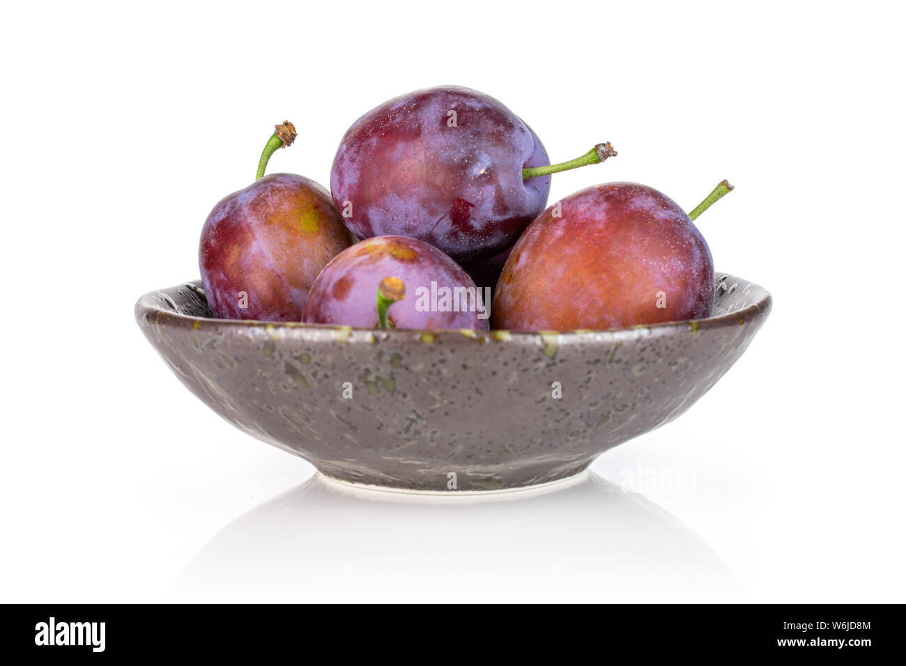 Group of four whole fresh blue plum in a dark ceramic bowl isolated on ...