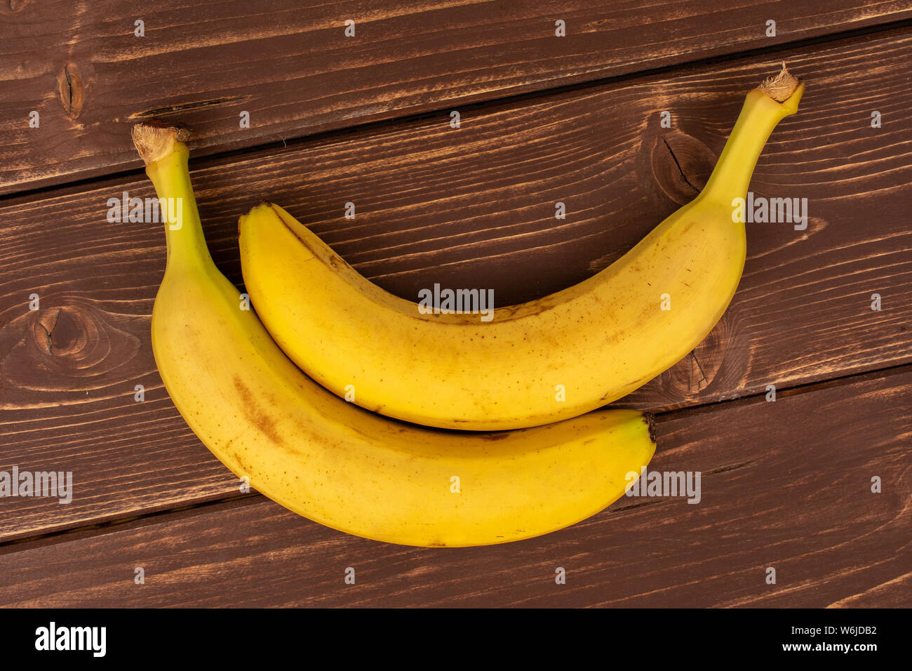 Group of two whole ripe yellow banana close together flatlay on brown ...