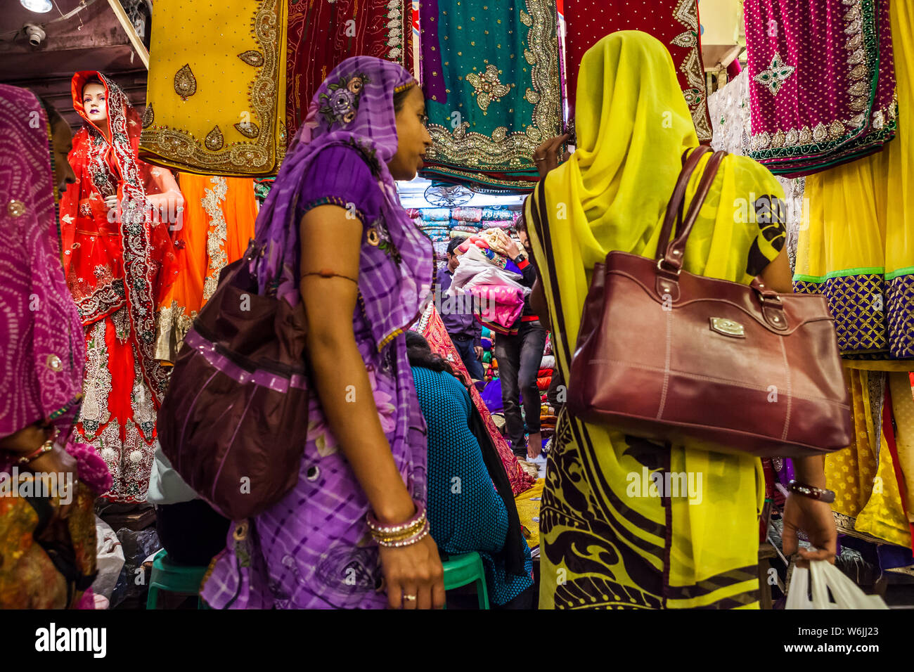 One woman looks at the camera in a Women walk by the many sari shops in ...