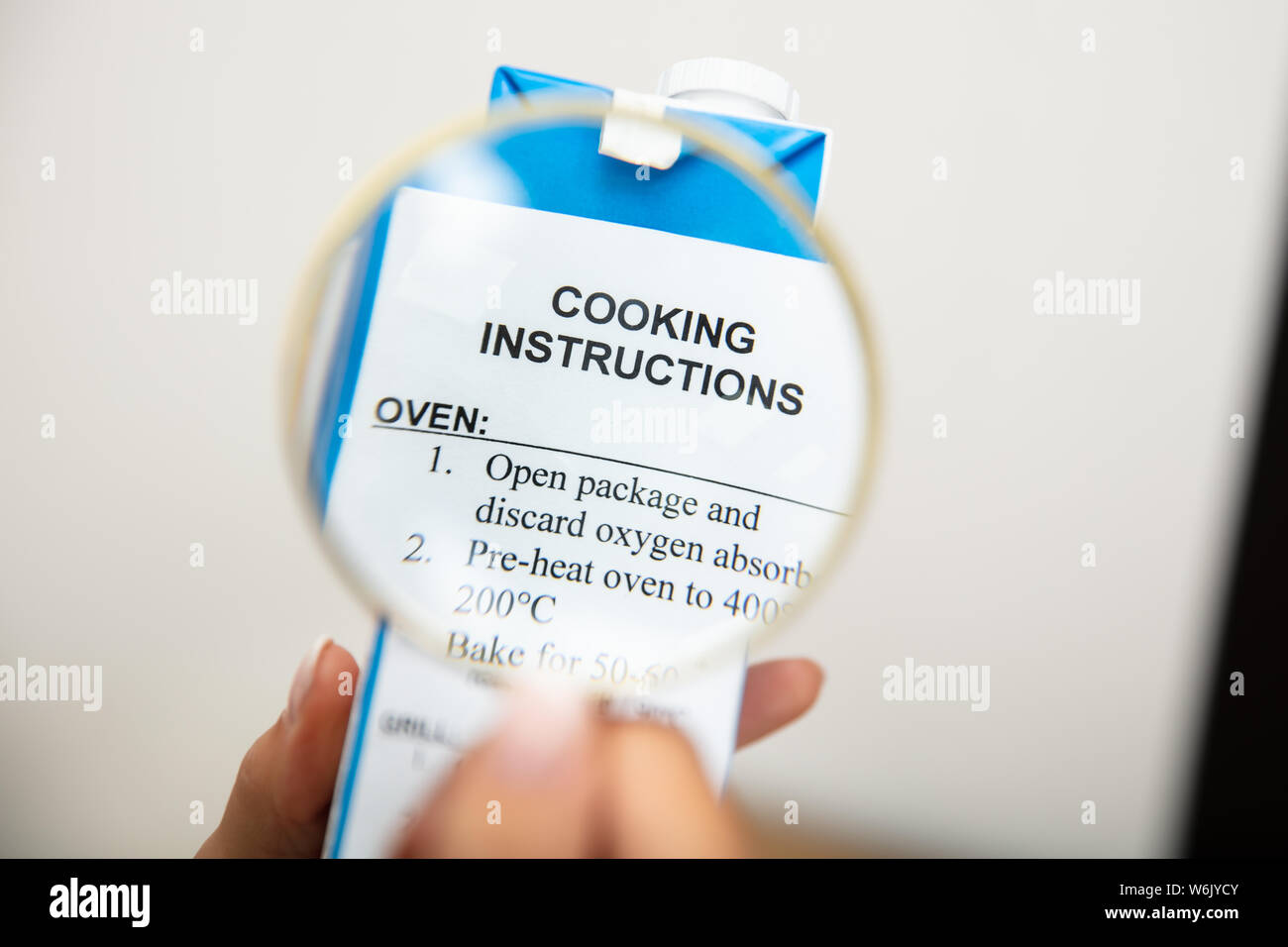 An Elevated View Of Person's Hand Holding Magnifying Glass Over Cooking ...