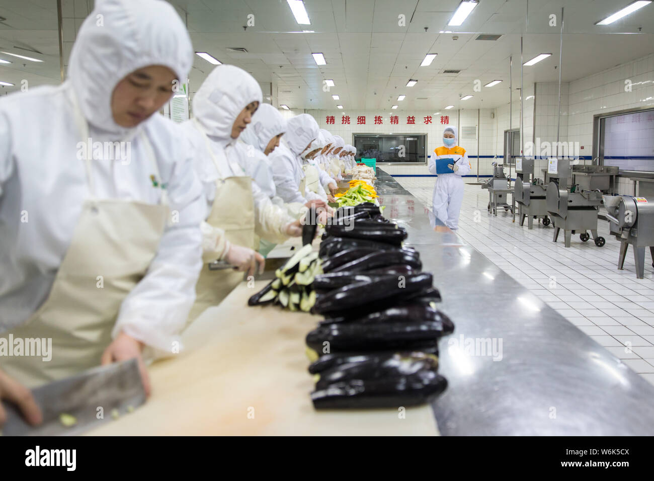A Chinese worker patrols as others cut up vegetables at a food ...