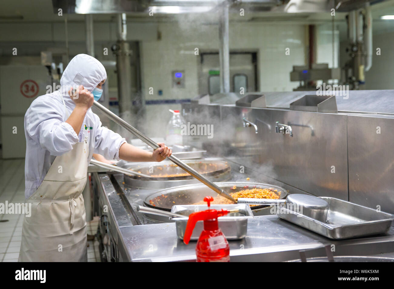 A Chinese worker stir-fries spicy diced chicken with peanuts at a food ...