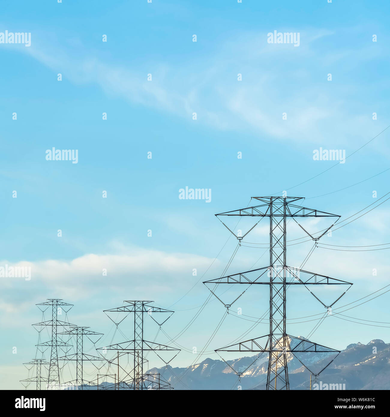 Square Towering power lines in the valley against snow capped mountain ...