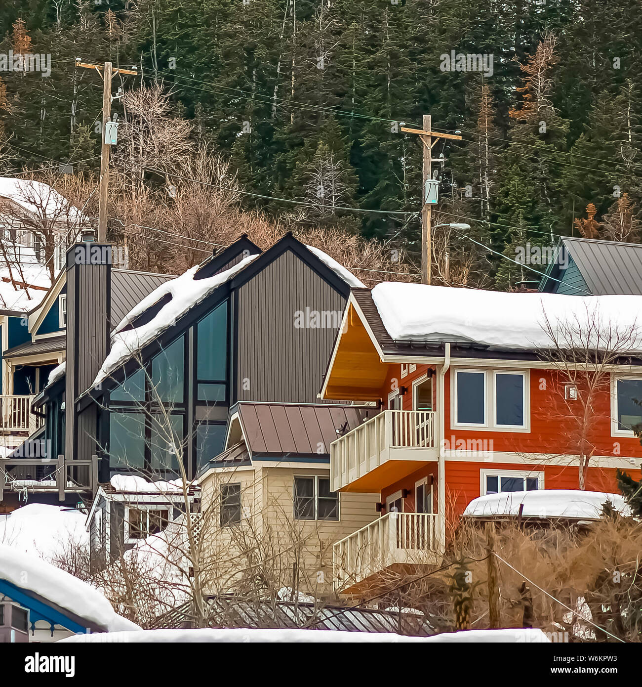 Square Mountain homes with snow covered roofs aginst coniferous trees ...