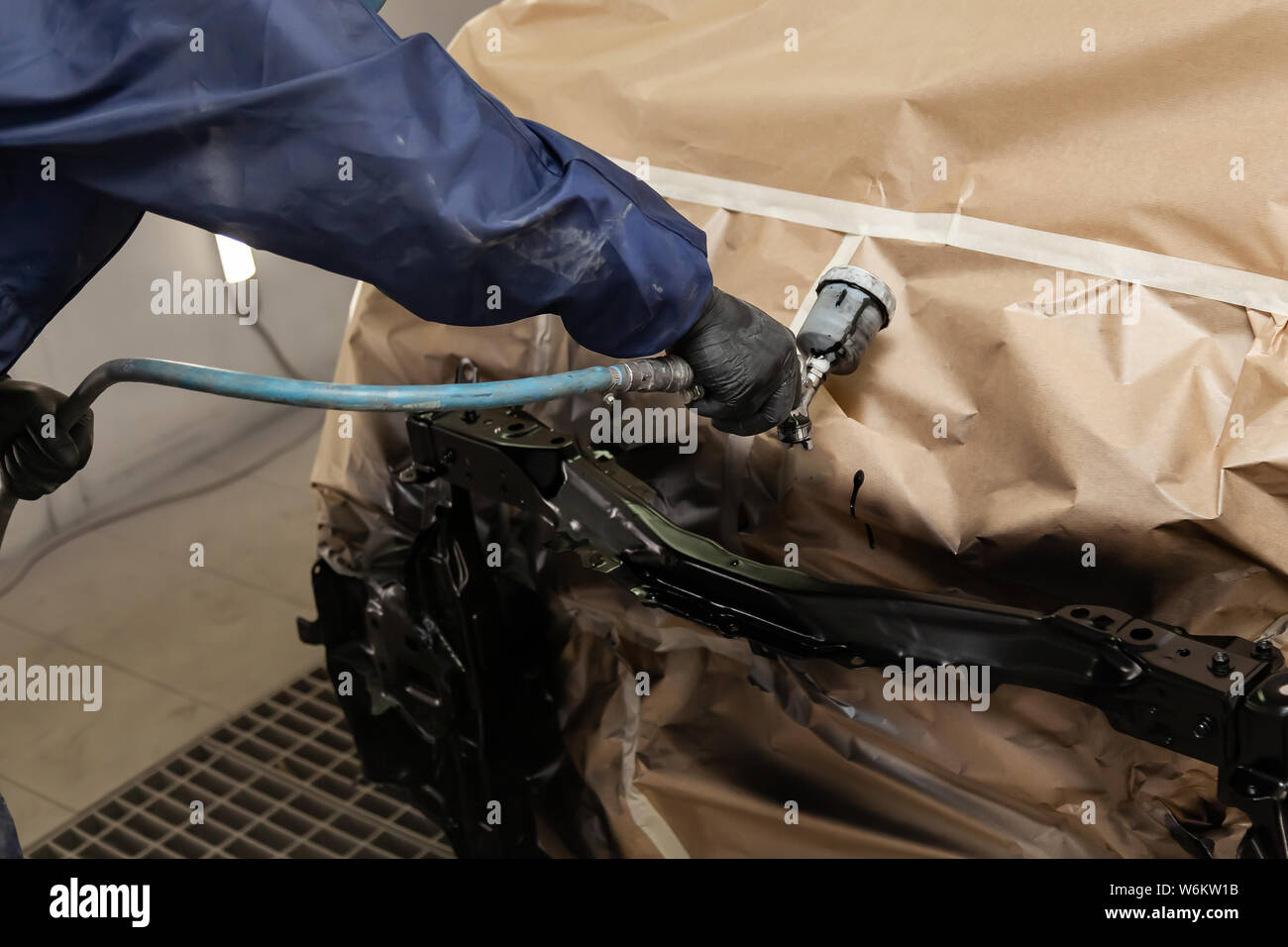 Painting a car frame black covered with paper in a body repair workshop ...
