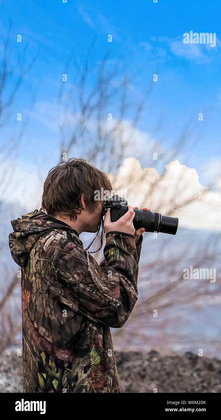 Vertical frame Side view of a man holding a camera with tree and cloudy ...