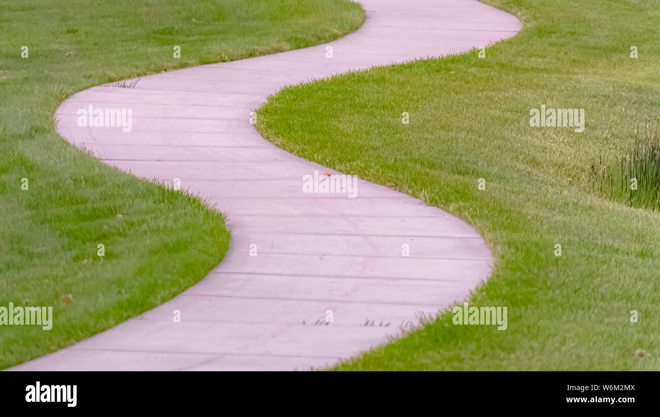 Pathway curving through grassy terrain with a pond and bench in the ...