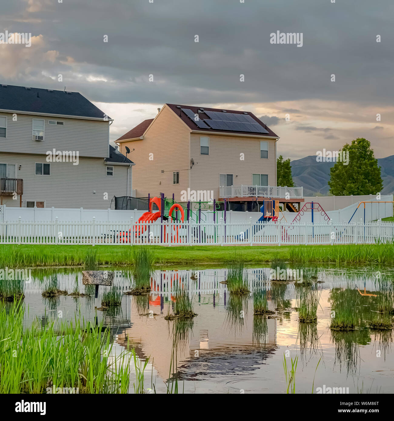 Square Shiny grassy pond with reflection of the playground homes cloudy ...