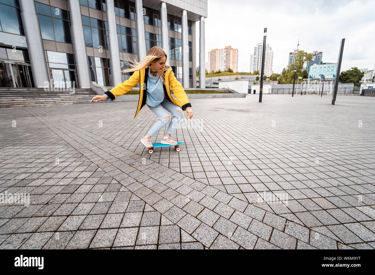 Blond female hipster woman riding on the longboard in the street at ...