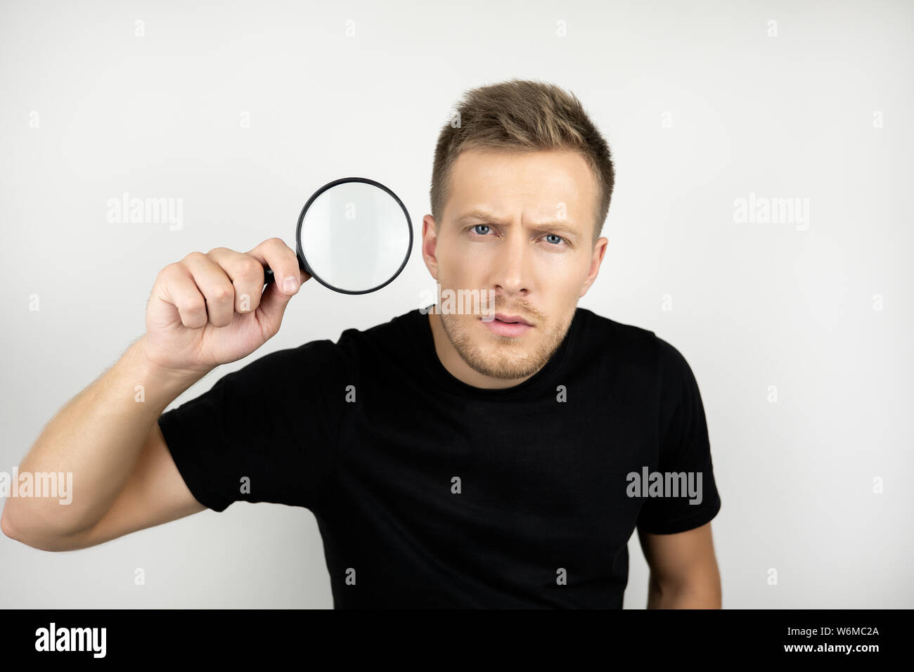 handsome young man wearing black t-shirt holding magnifying glass near ...