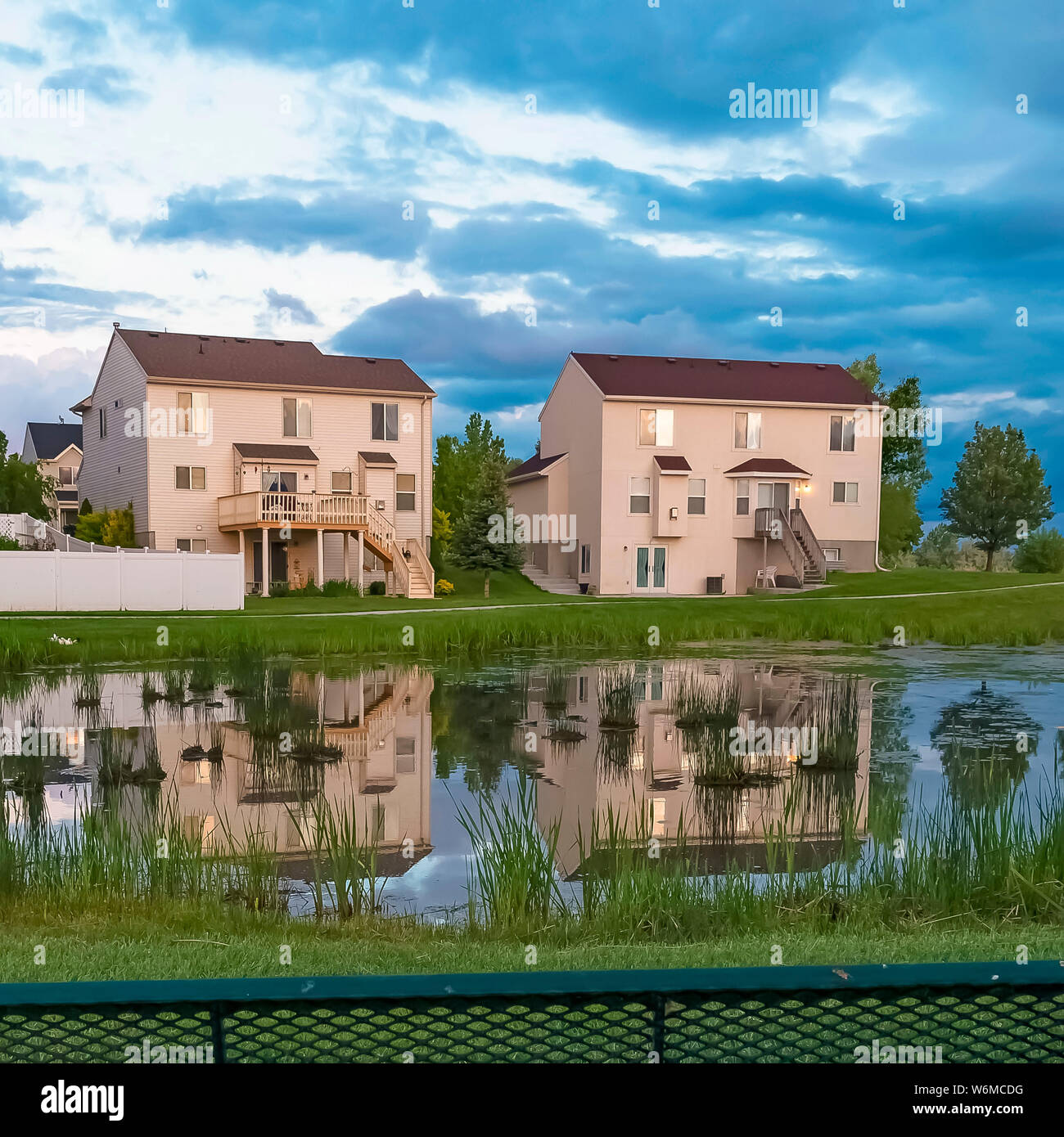 Square Green metal bench facing a shiny pond with reflection of homes ...