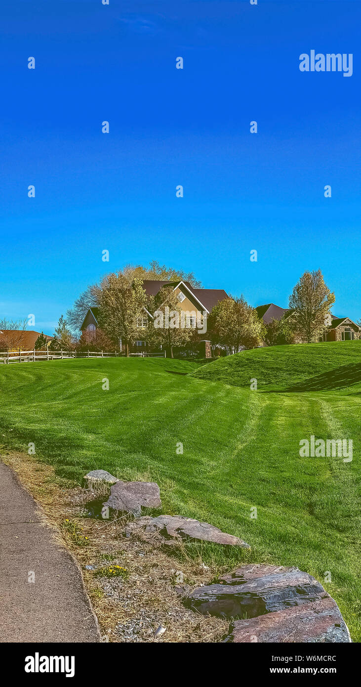 Vertical Narrow paved road on a vast grassy terrain under blue sky on a ...