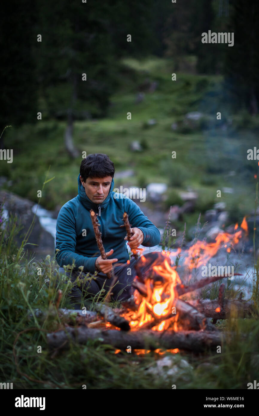 Young man making fire while camping outdoors, in an alpine wilderness ...