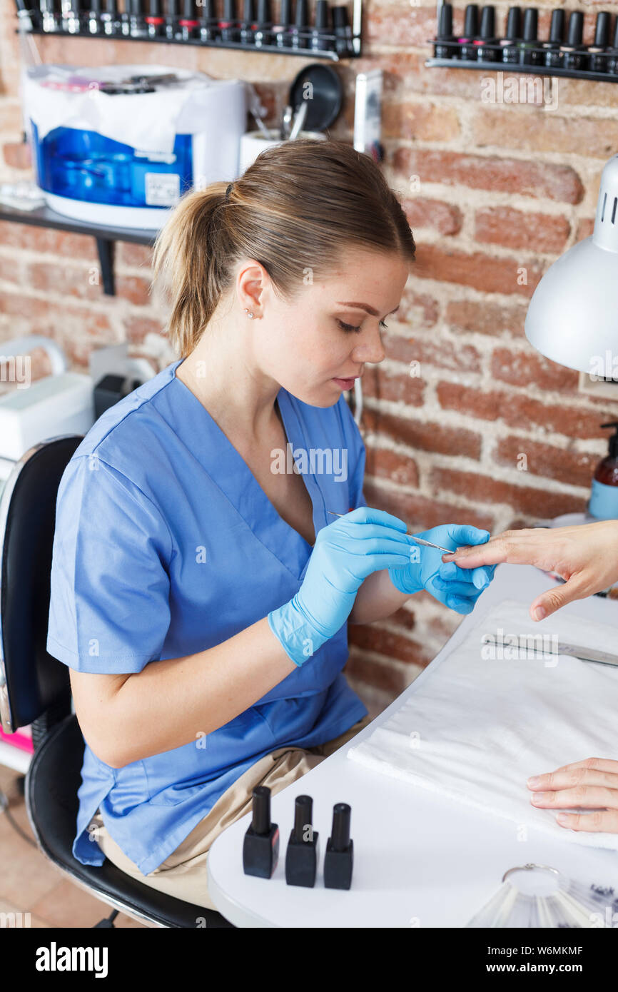 Professional manicurist doing manicure by nail to girl in modern beauty ...