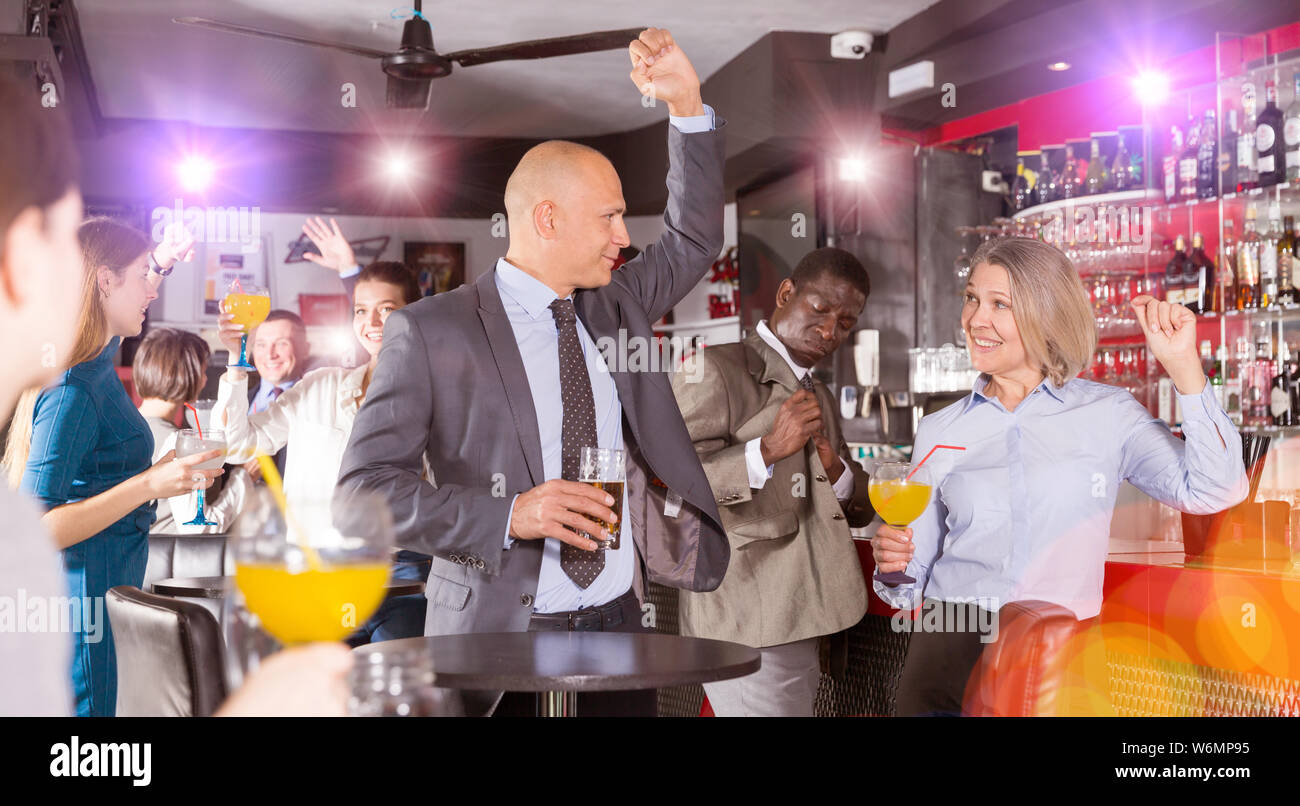 Cheerful businessman with female colleague dancing and drinking alcohol ...