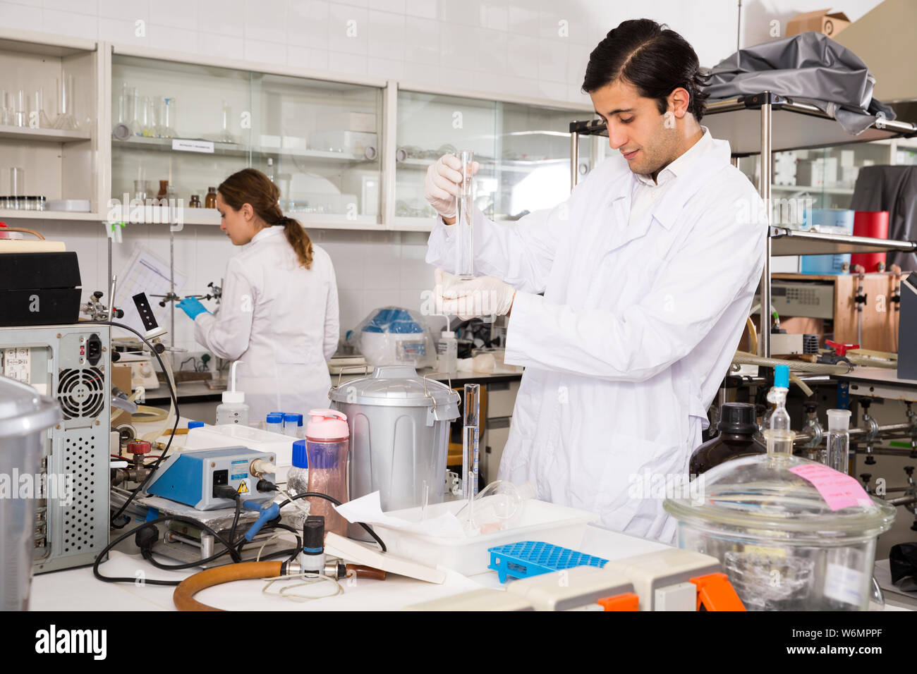 Focused young lab technician working with reagents in test tubes during ...