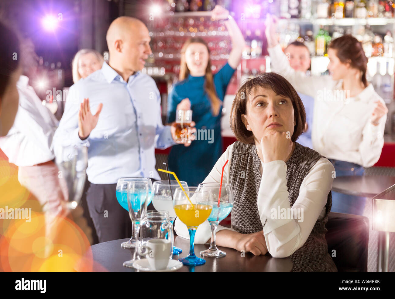 Sad woman sitting alone at office party in nightclub in background with ...