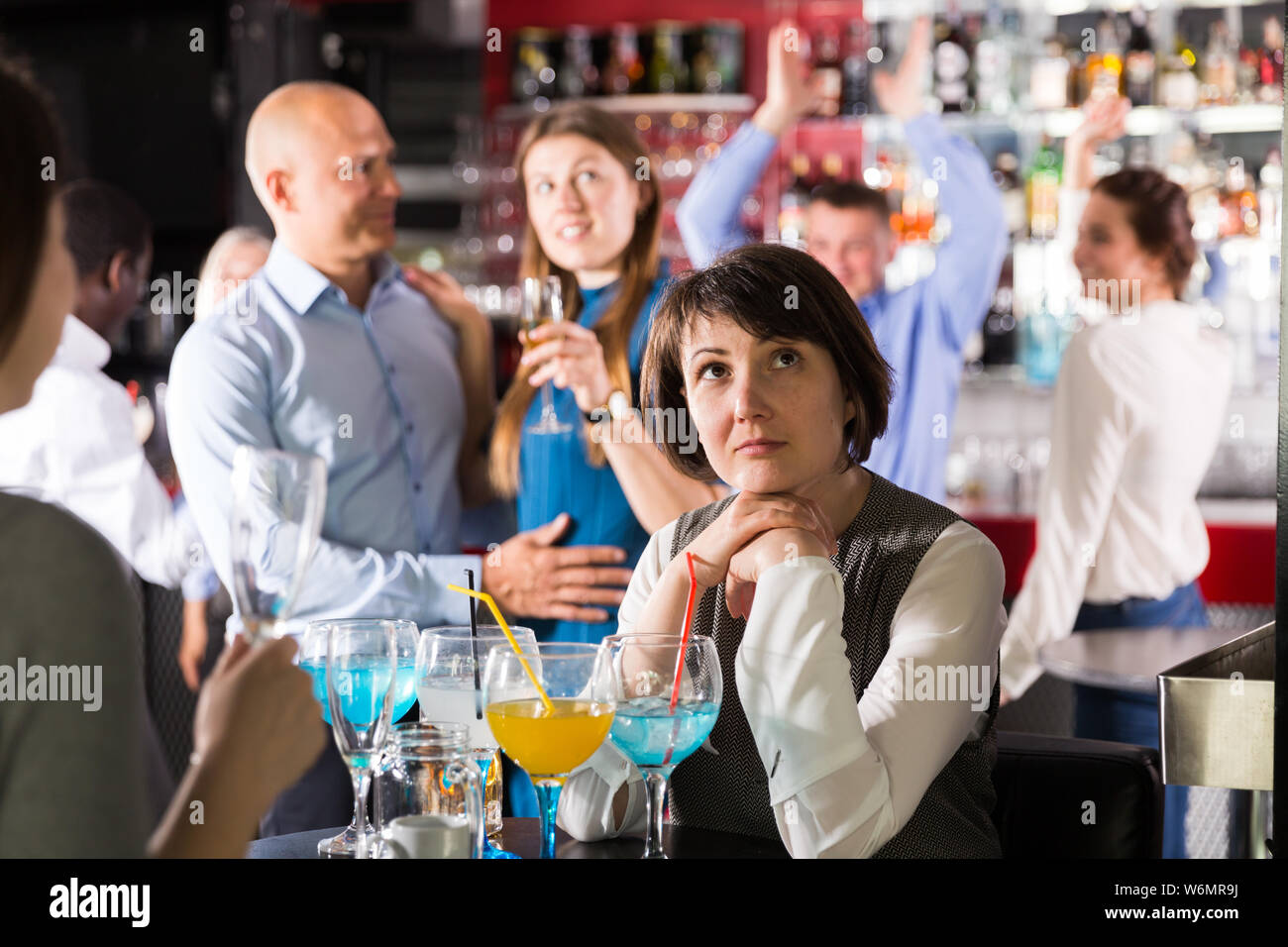 Sad woman sitting alone at office party in nightclub in background with ...