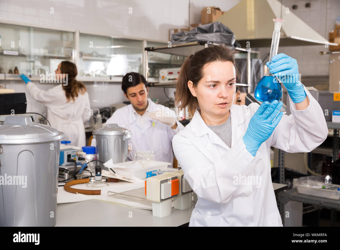 Focused woman lab technician working with reagents in test tubes during ...