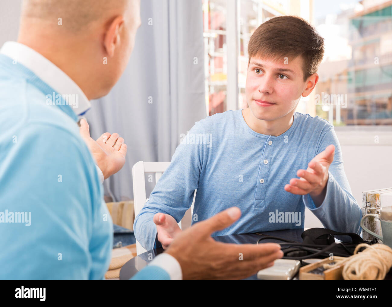 Portrait of teen boy having conversation with man in home interior ...